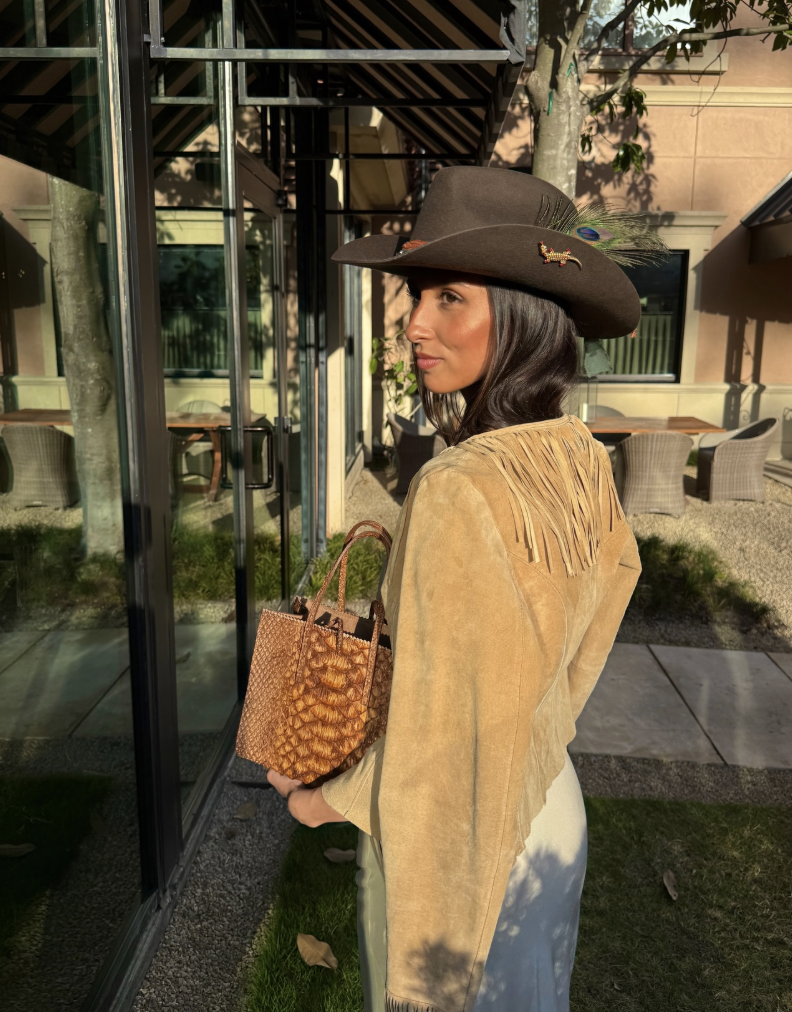Soft suede fringe jacket paired with a light blue dress%2C accessorized with a woven brown handbag and a wide-brimmed hat.